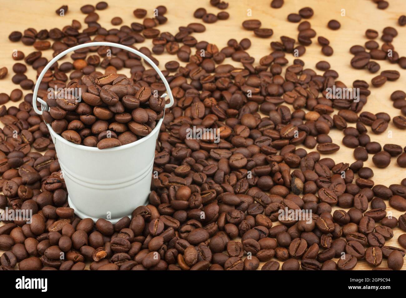 White bucket with coffee beans on the wooden floor, as a background ...