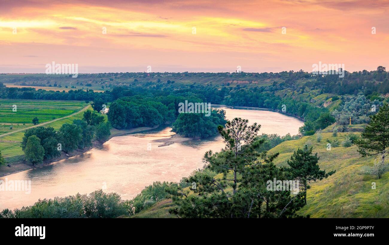 Aerial shot of river flowing along the rural landscape fields at sunset ...