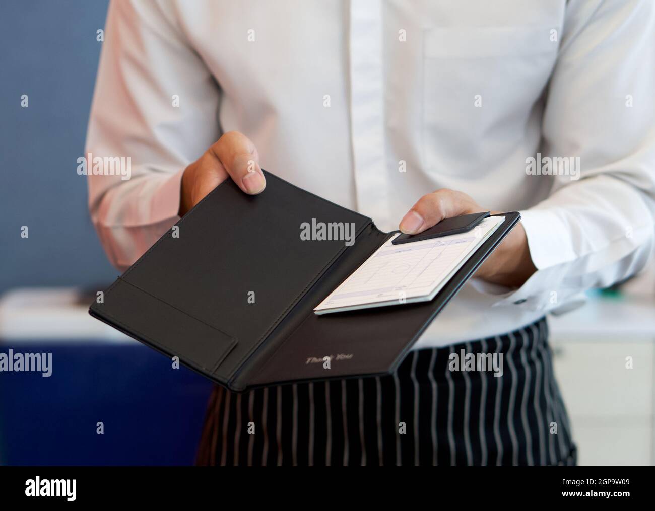 The waiter in a white shirt and apron presents a receipt after calling ...