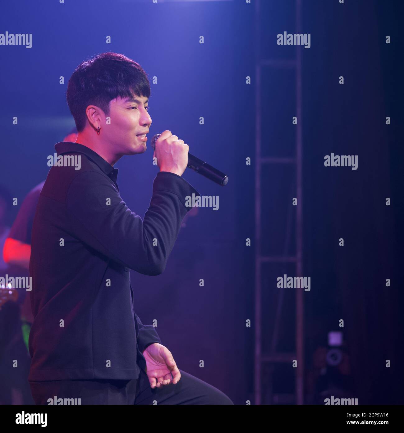 Young black-haired asian singer with a microphone singing on stage. The ...