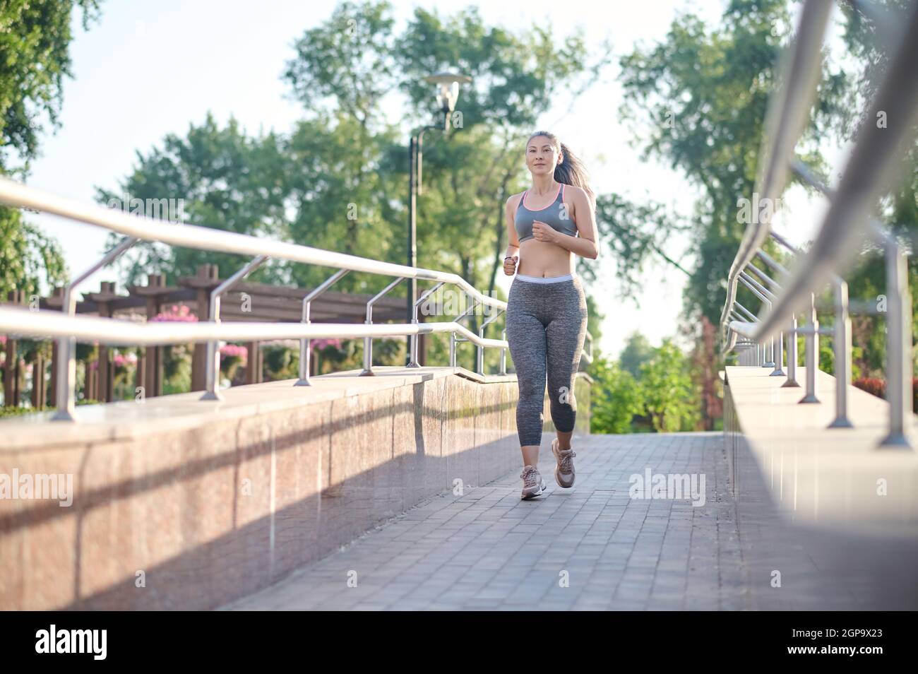 A woman in grey sportswear jogging in the park Stock Photo - Alamy