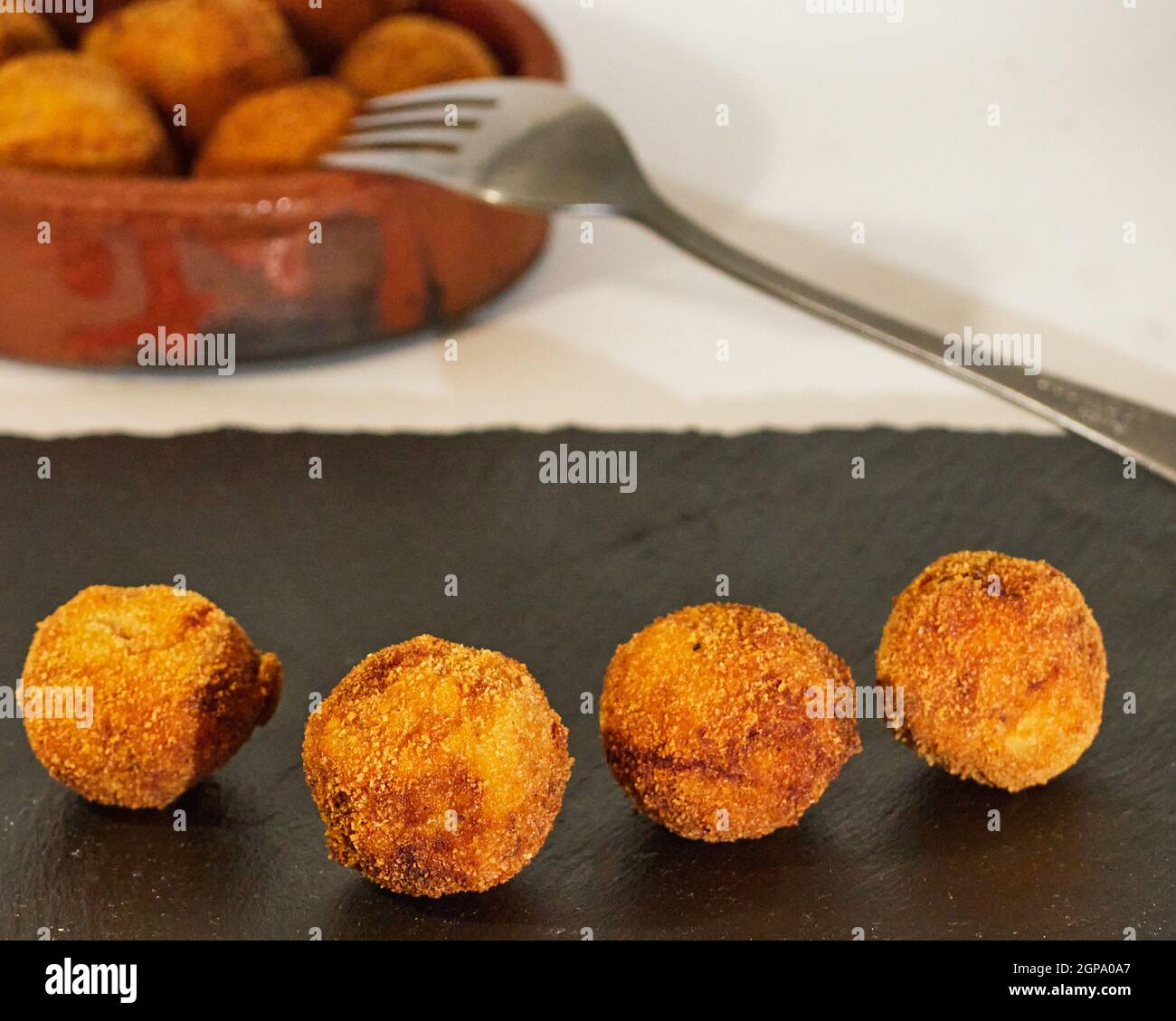 4 round croquettes on a black slate board decorated with a croquettes ...