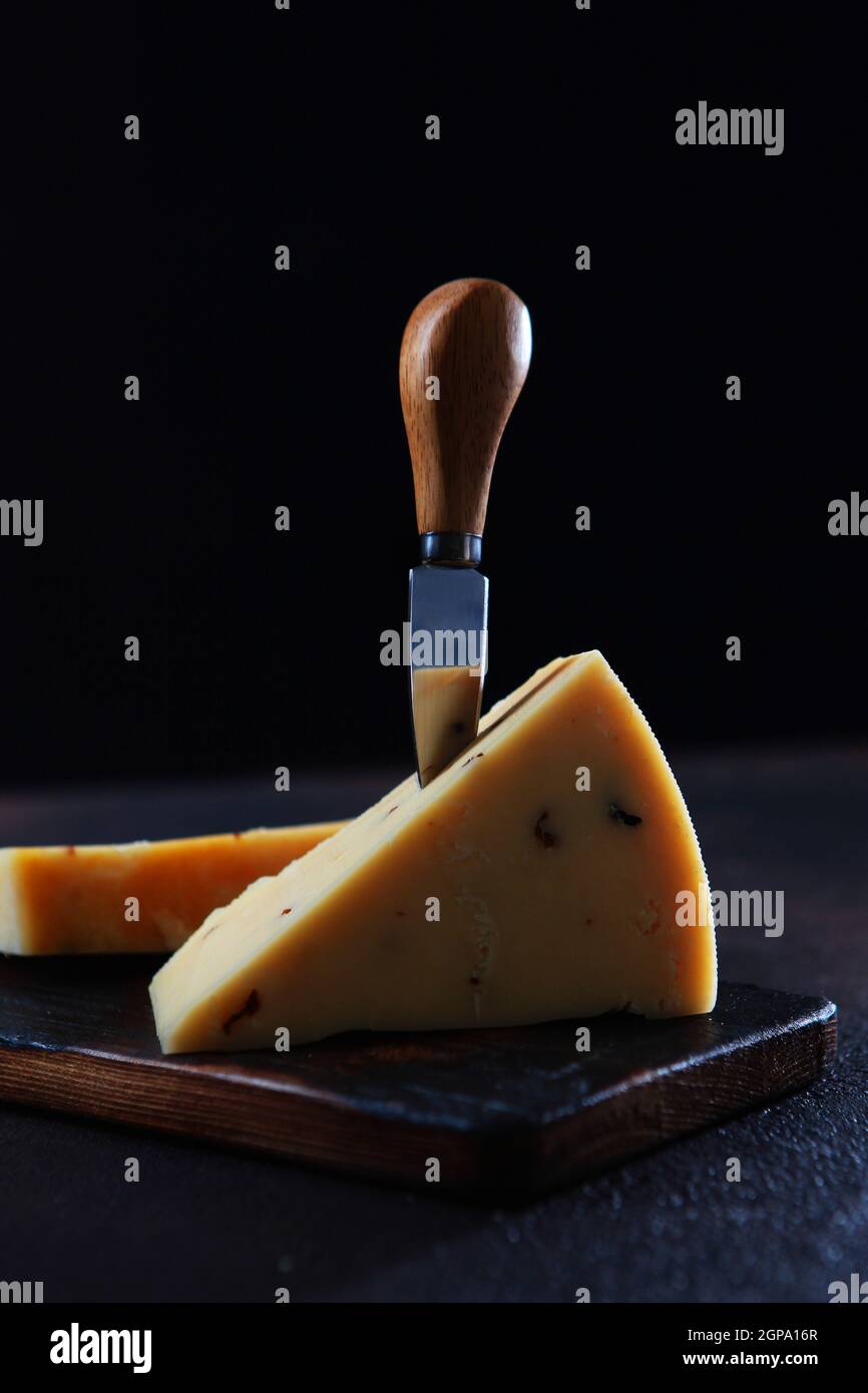 A piece of hard cheese and a cheese knife . Dairy product. Craft cheese ...