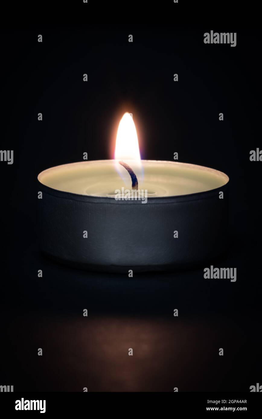 A burning candle on a dark background with a flare in the foreground ...