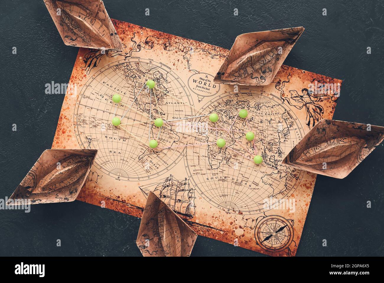 Paper boats, world map and pins on dark background Stock Photo - Alamy