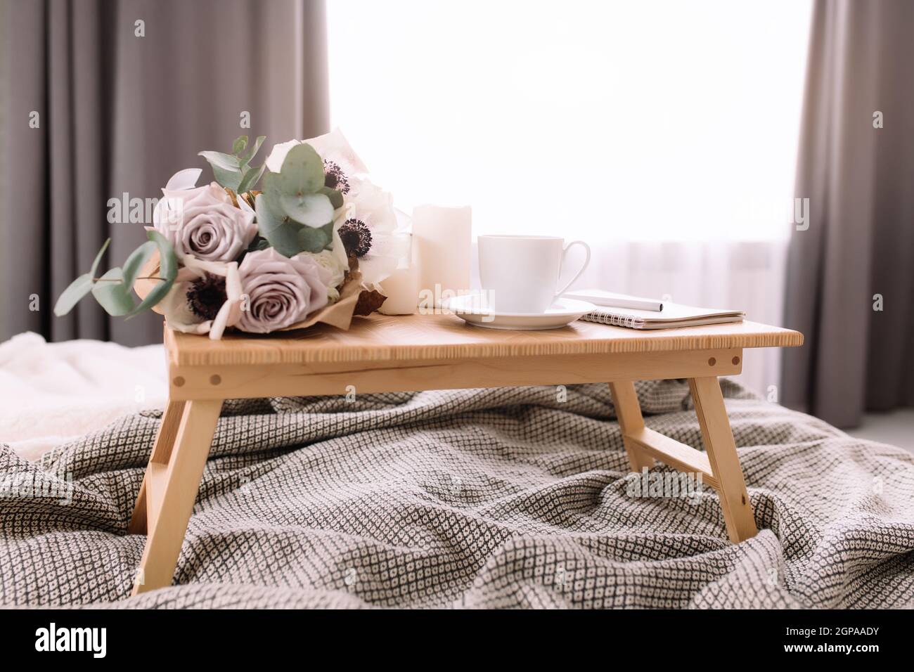 Romantic morning. Wooden coffee table with flowers on bed with plaid ...