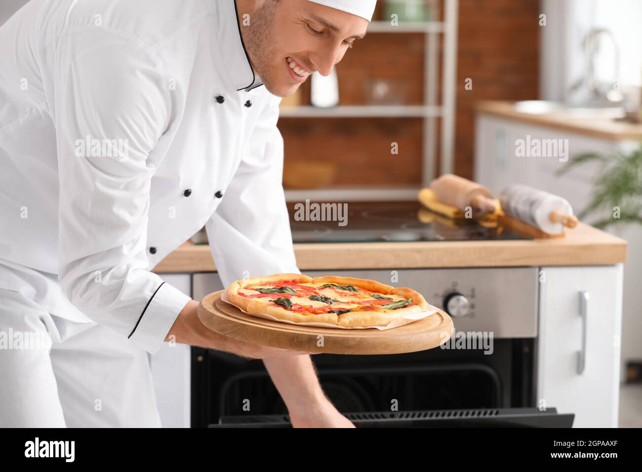 Italian chef taking tasty pizza from oven in kitchen Stock Photo - Alamy