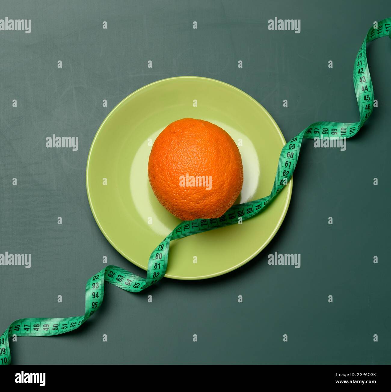 orange wrapped in green measuring tape on a round plate, slimming ...