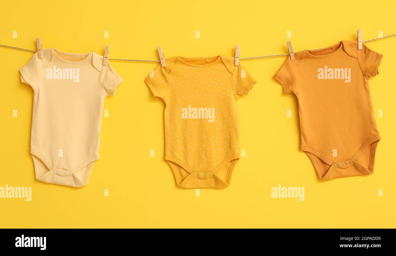Stylish baby clothes hanging on rope against yellow background Stock ...