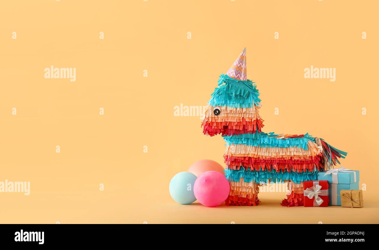 Mexican pinata with party hat, gifts and balloons on color background ...