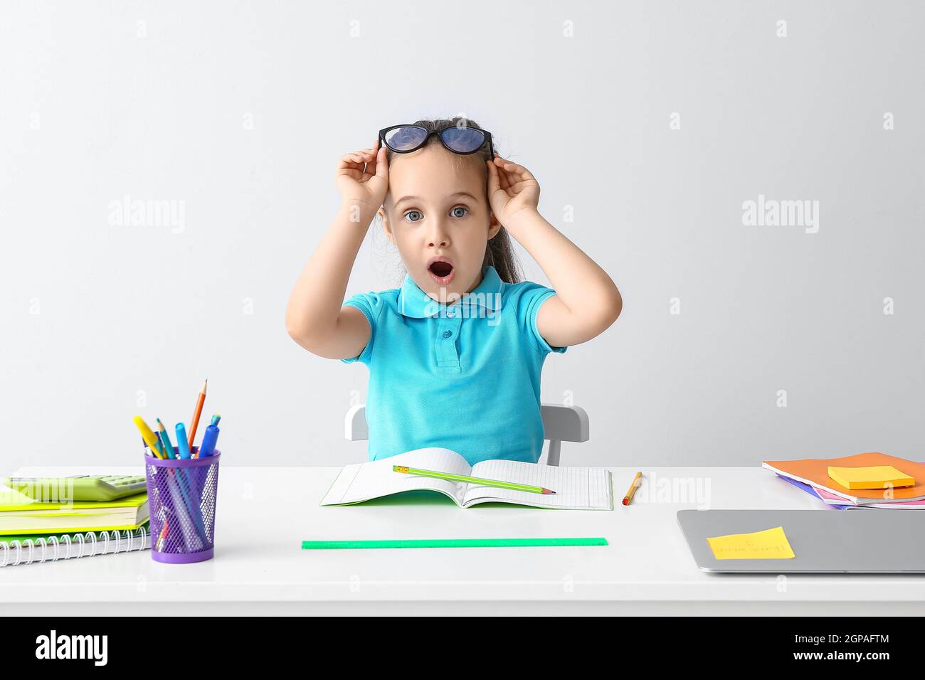 Shocked little girl doing homework at table on light background Stock ...