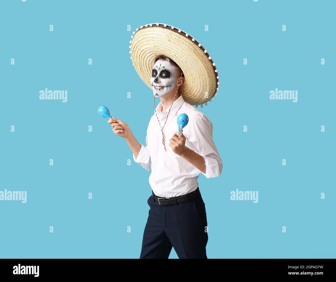 Young man with painted skull on his face and maracas against color ...