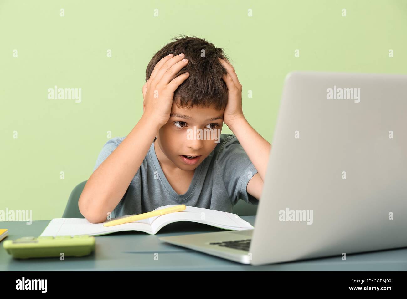 Stressed little boy doing homework at table on color background Stock ...