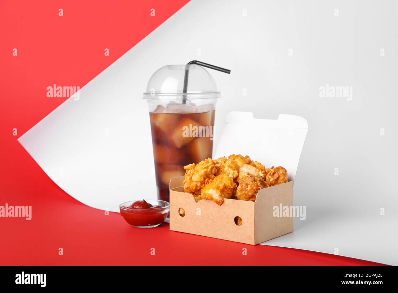 Paper box with fried popcorn chicken and plastic cup of cola on color ...
