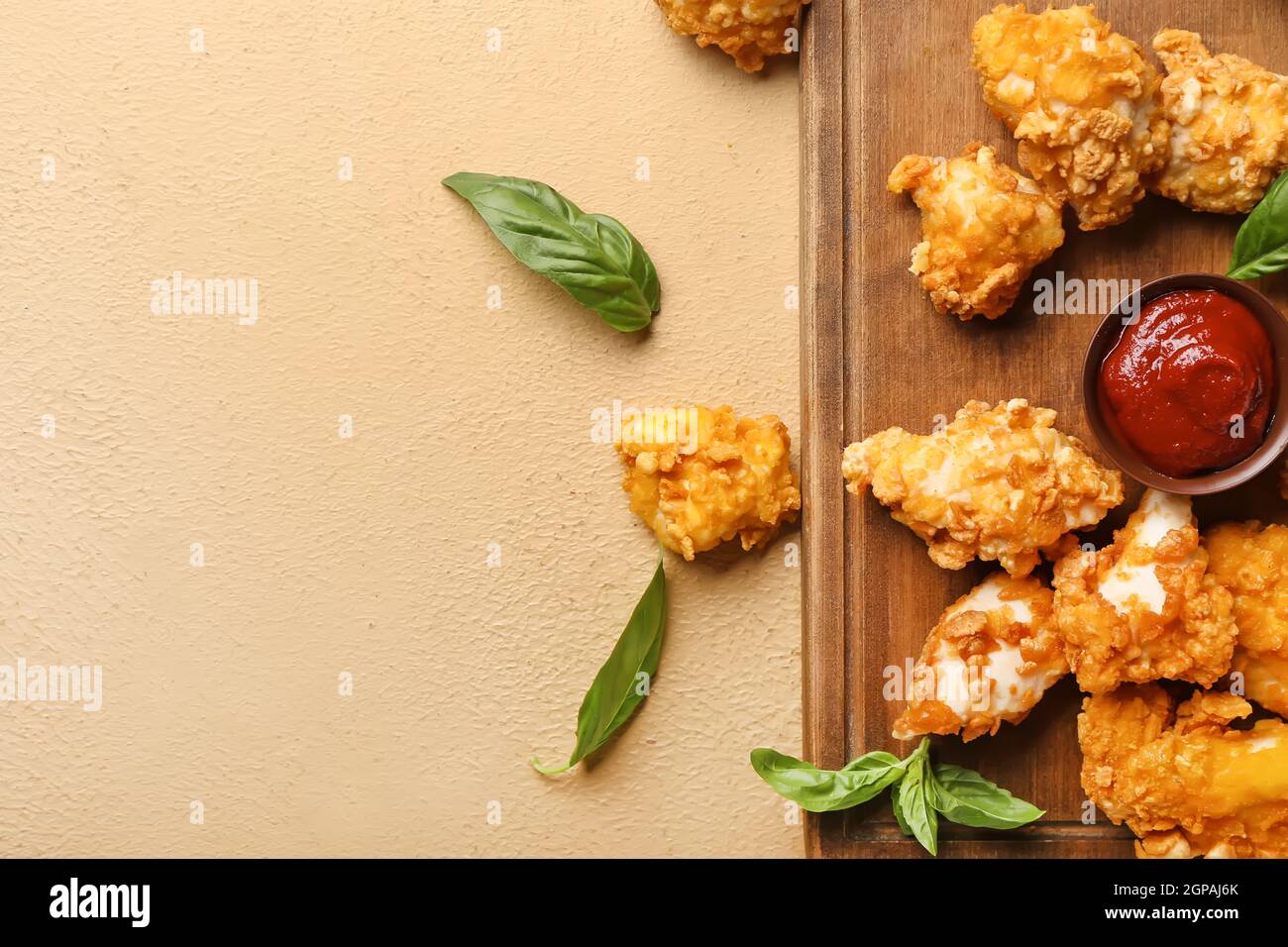 Board with tasty popcorn chicken, sauce and basil on color background ...