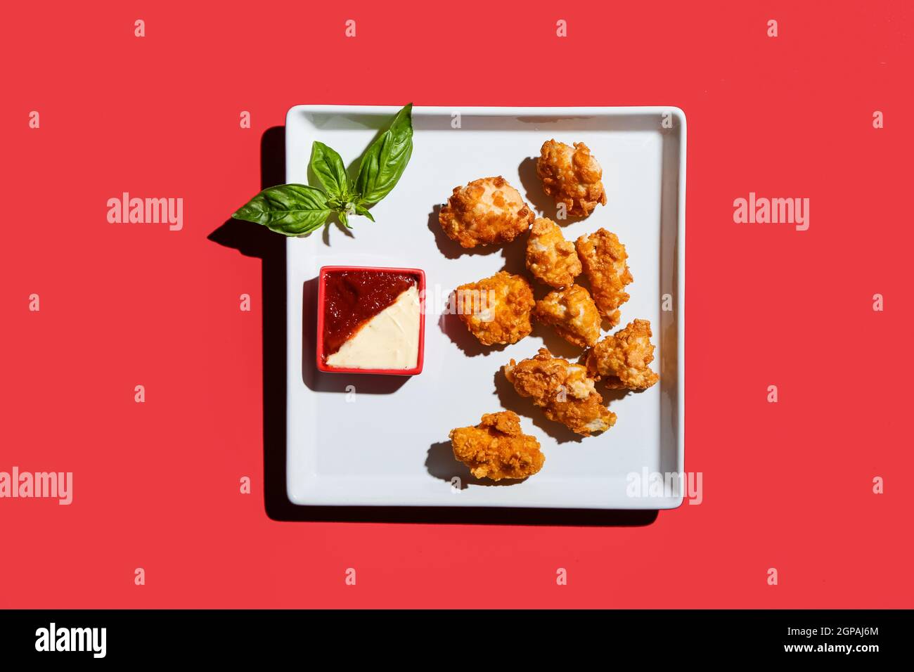 Plate with tasty popcorn chicken, sauces and basil on color background ...