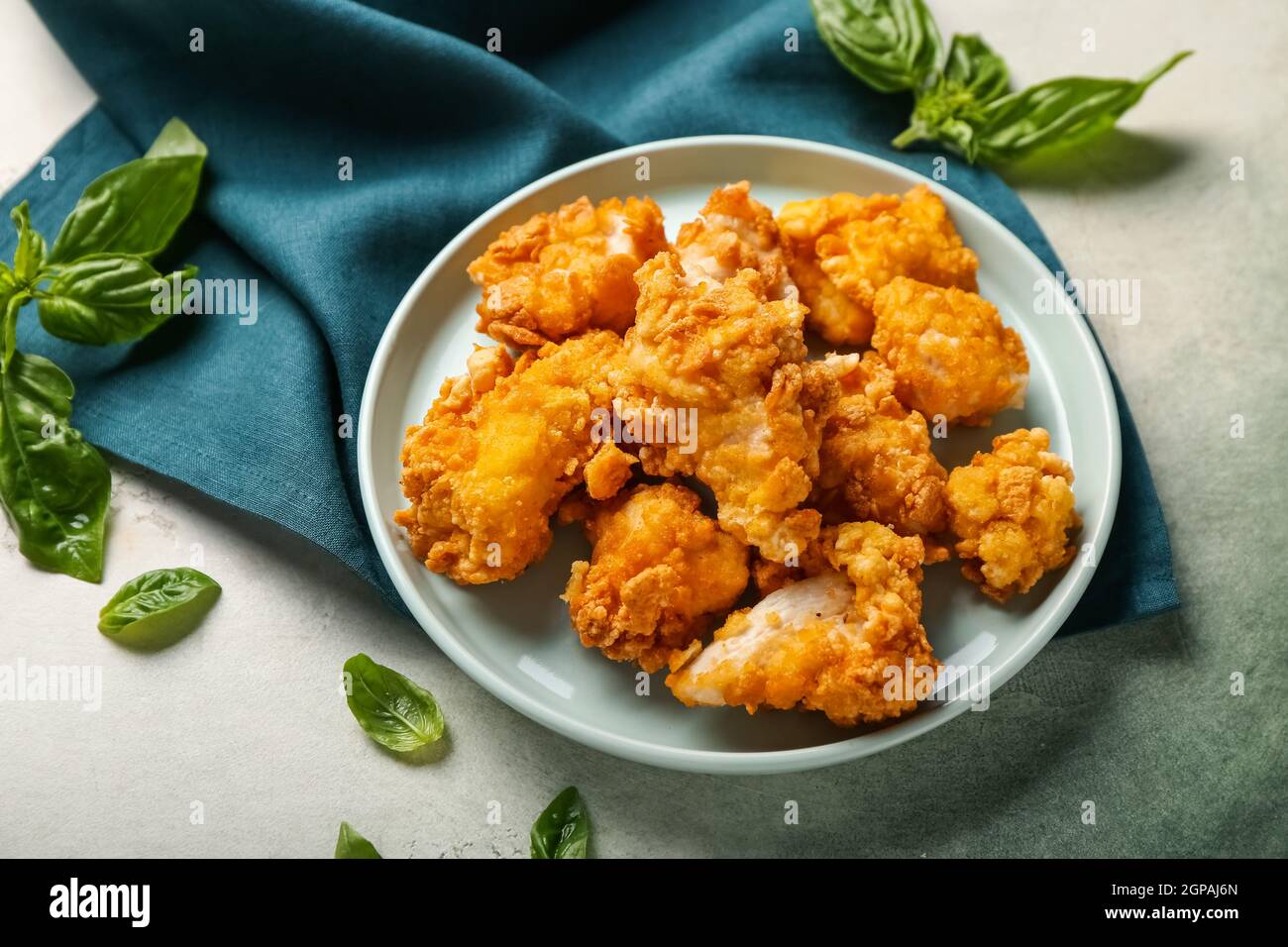 Plate with tasty fried popcorn chicken and basil on color background ...