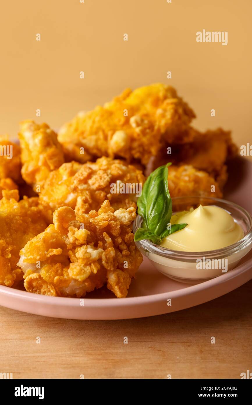 Plate with popcorn chicken, sauce and basil on color background ...