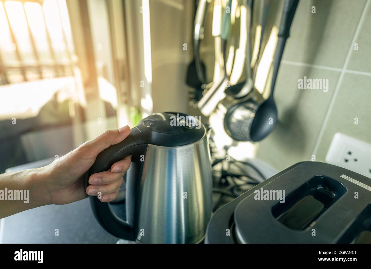 Woman hand holding handle of electric kettle in apartment kitchen ...