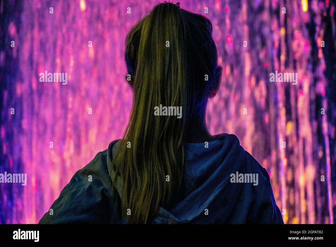 Rear view of a young female kid facing at the purple neon lights ...