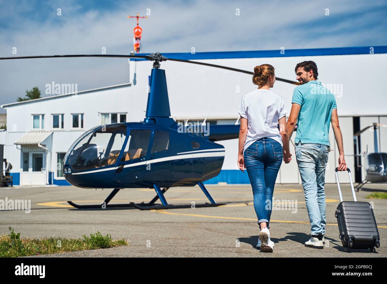 Two air travelers with baggage approaching helicopter Stock Photo - Alamy