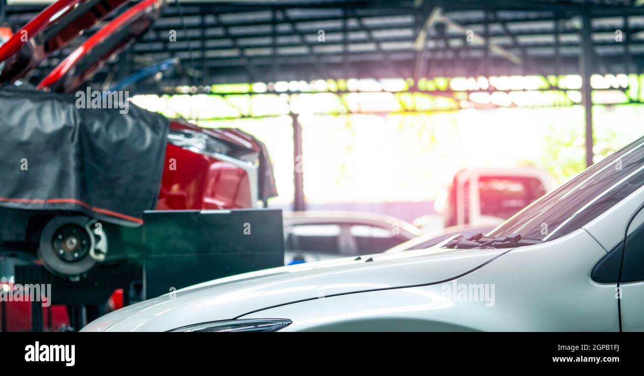 Auto repair shop. White car on blurred red SUV lifted in garage for ...
