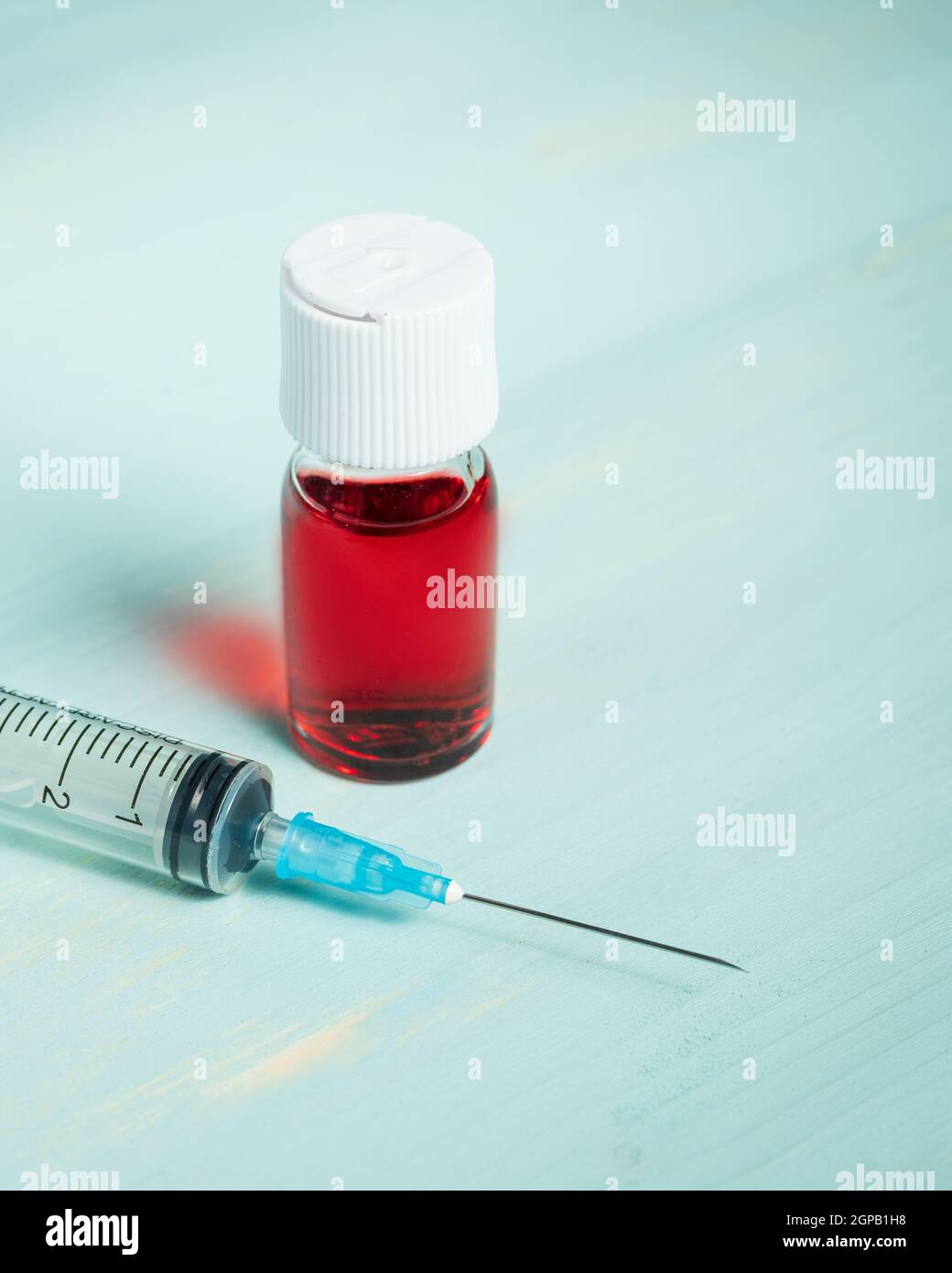 medical vaccine ampule with red liquid and syringe over green table and ...