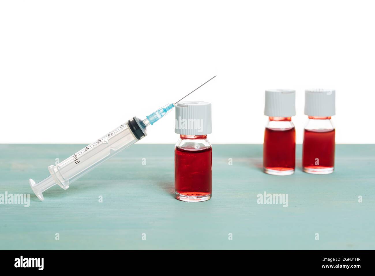 medical vaccine phials with red liquid and syringe over green table and ...