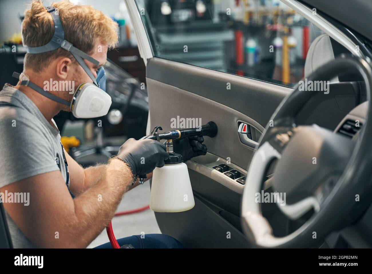 Man in respirator mask do chemical cleaning of steering wheel closeup ...