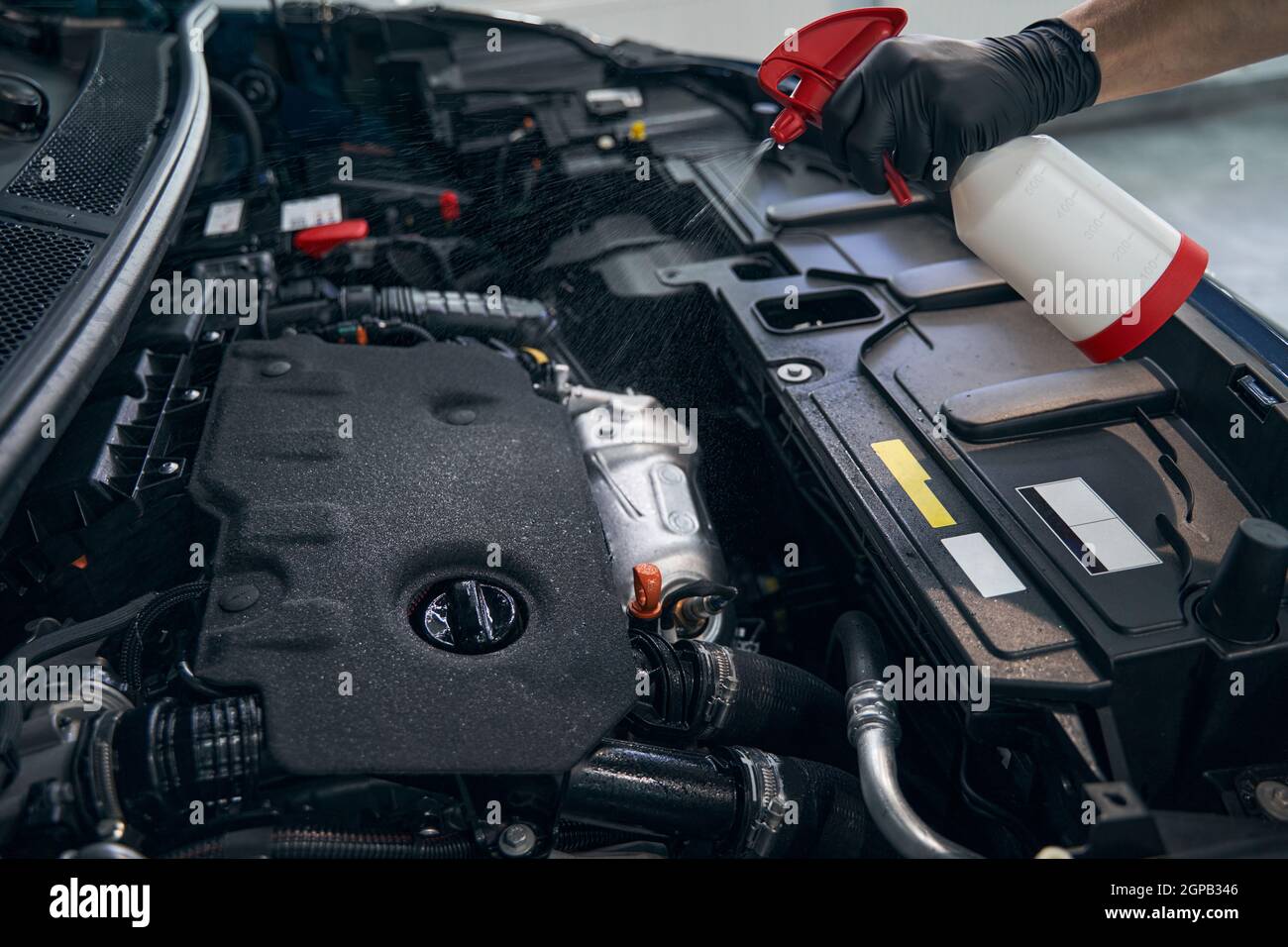 Mechanic in gloves clean car engine with spray at auto service station ...