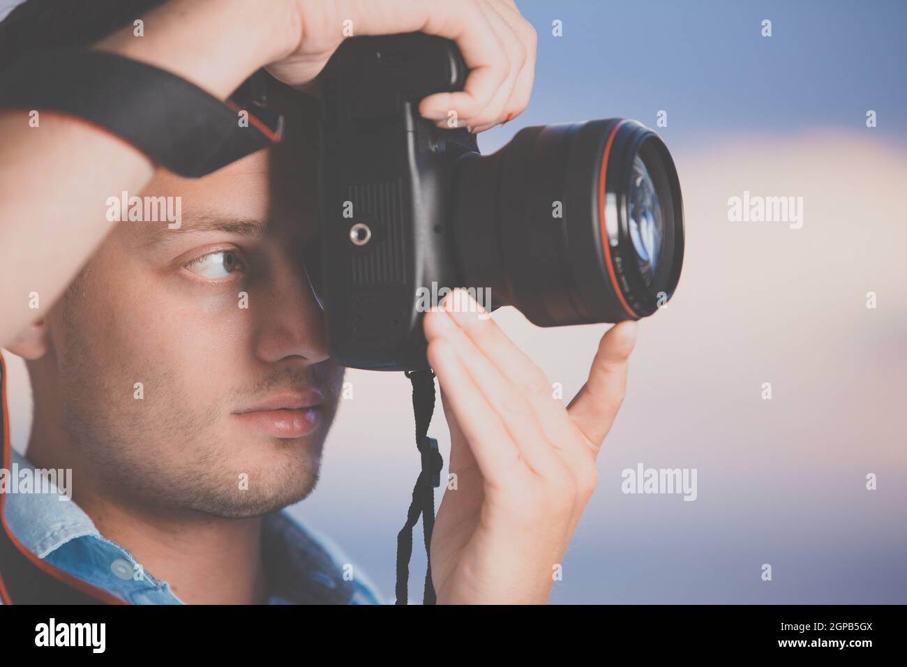Handsome young photographer using his modern DSLR outdoors, against ...