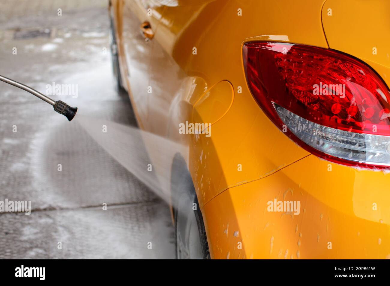 Rear wheel and back of yellow car being washed with jet water stream in ...