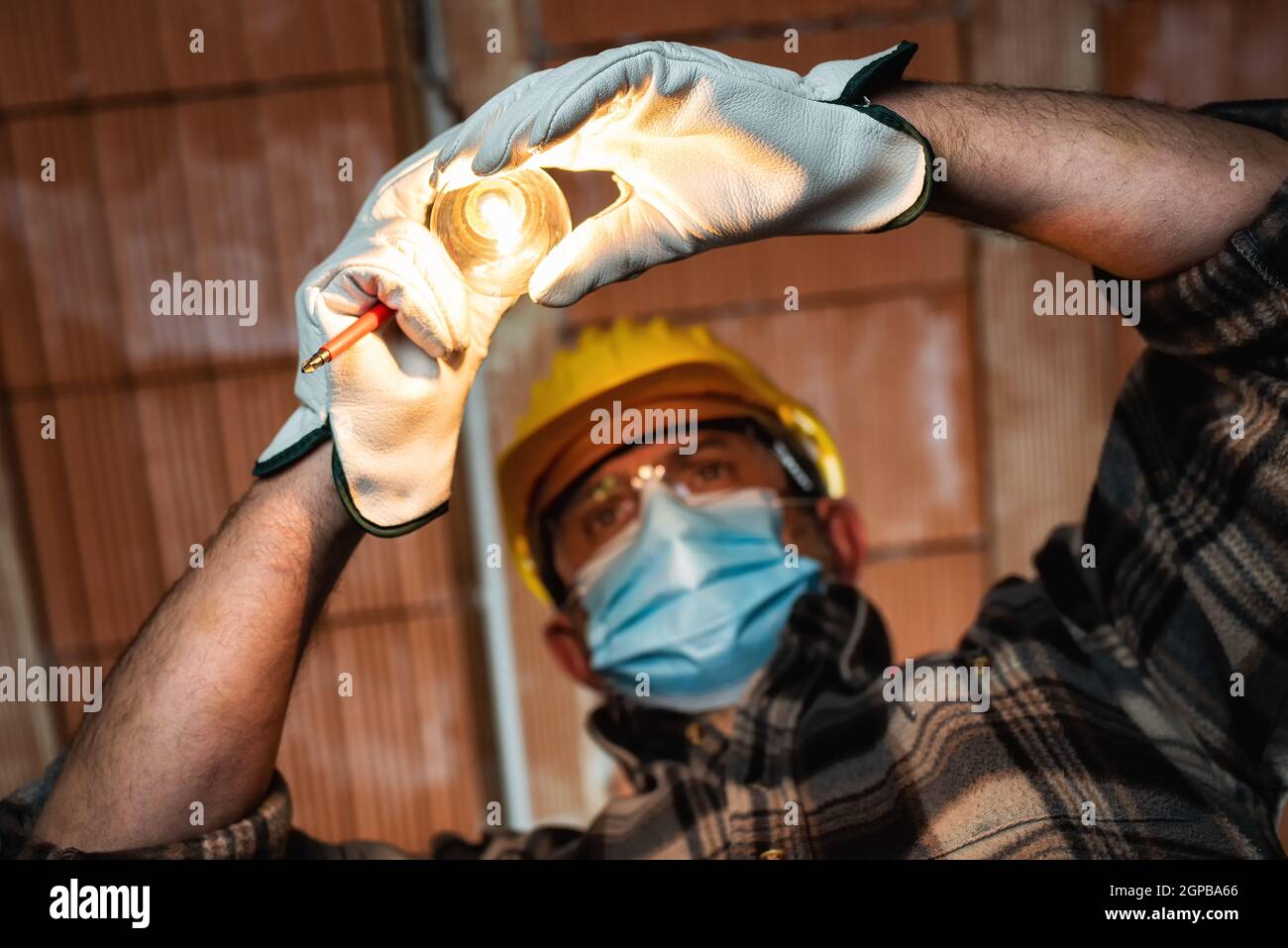 Electrician worker at work replaces the light bulb protected by helmet ...
