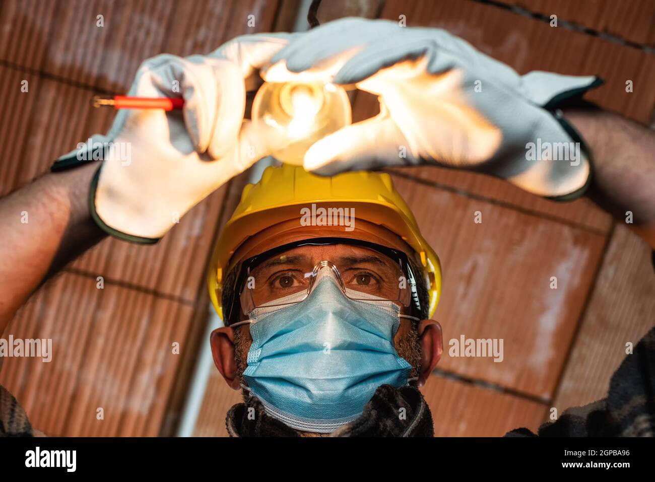 Electrician worker at work replaces the light bulb protected by helmet ...