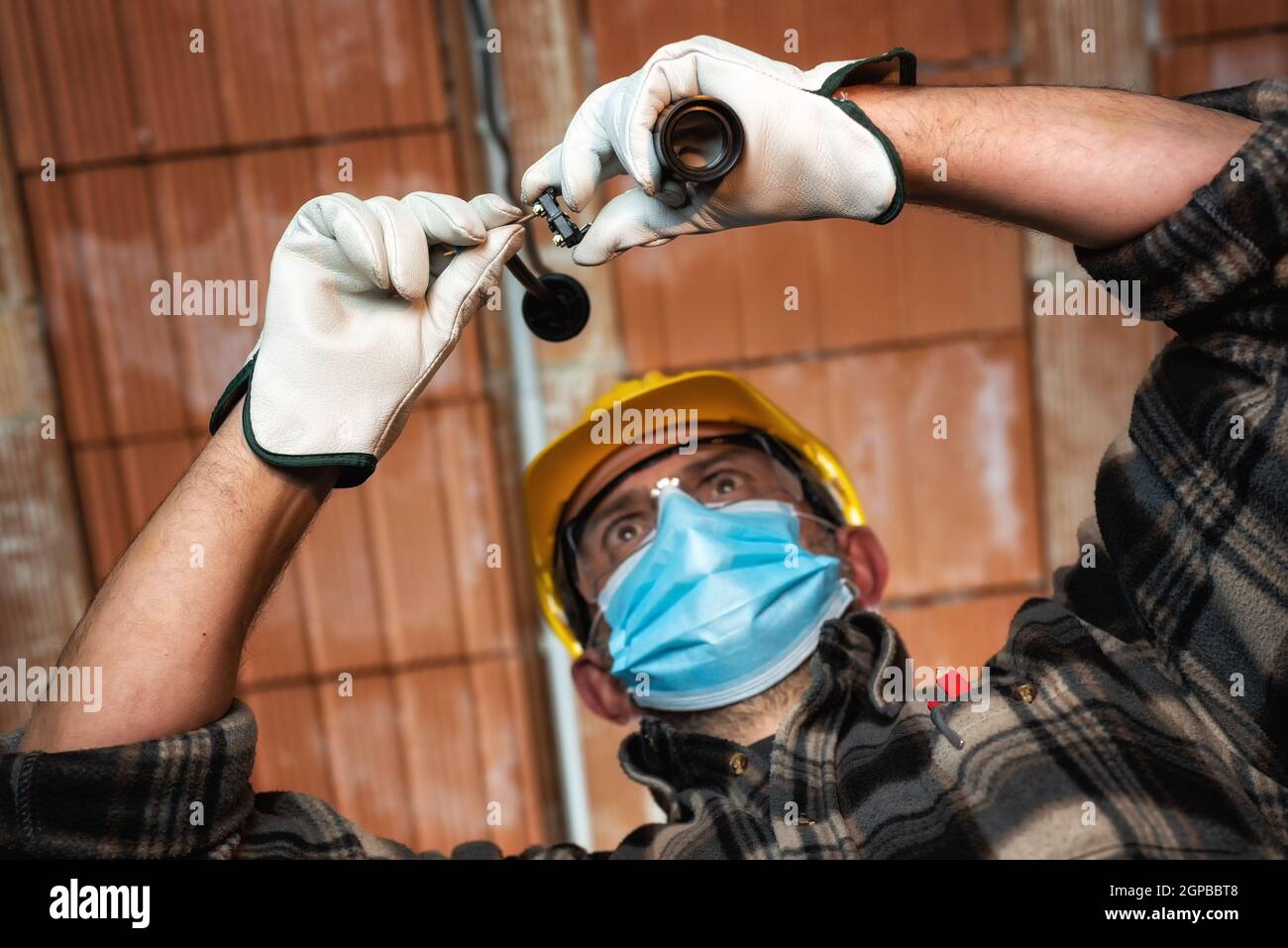 Electrician worker at work replaces the lamp holder protected by helmet ...