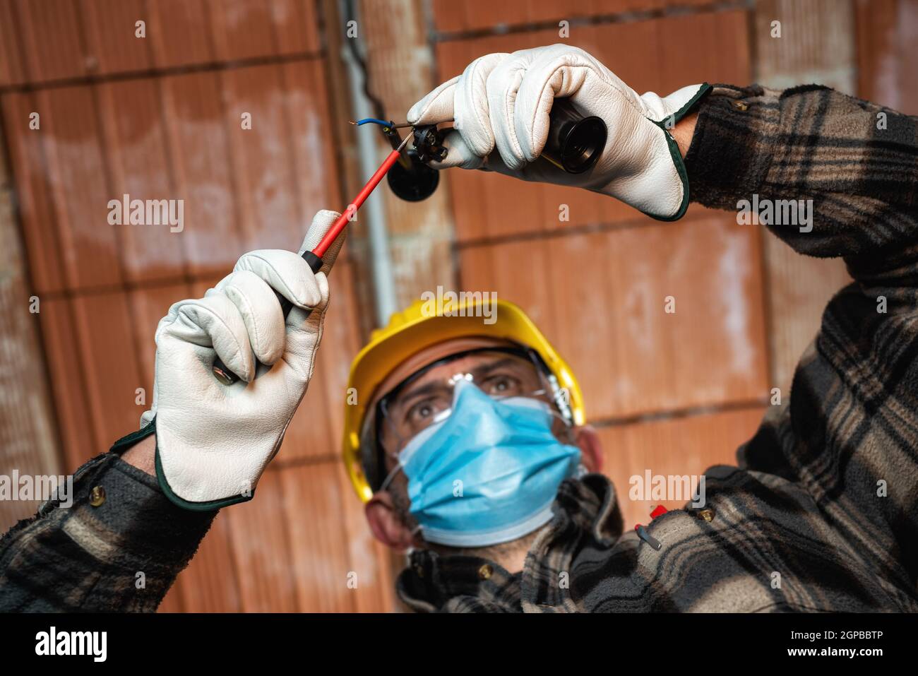 Electrician worker at work replaces the lamp holder protected by helmet ...