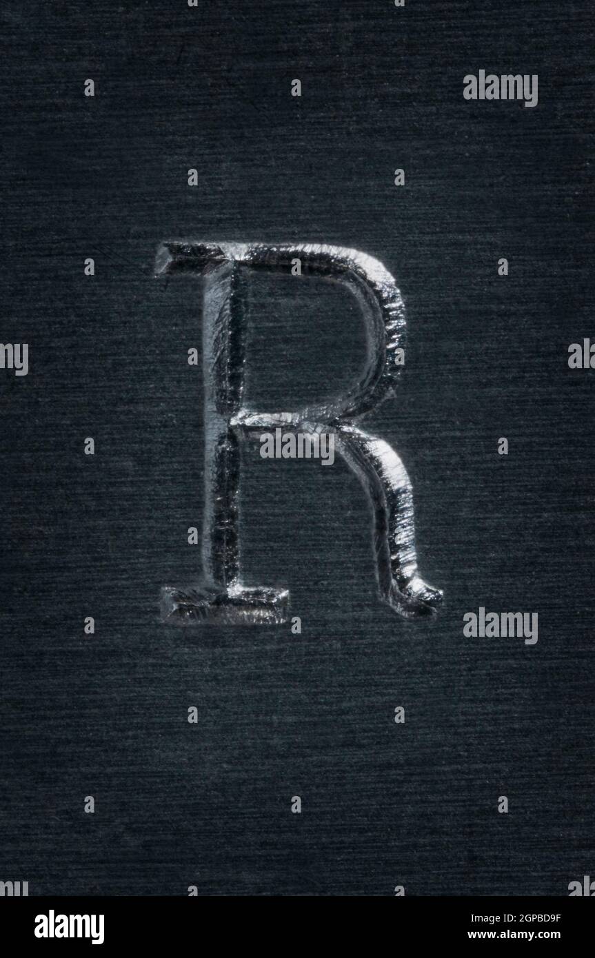Detailed view of the letter R embossed into a gray and sanded steel ...