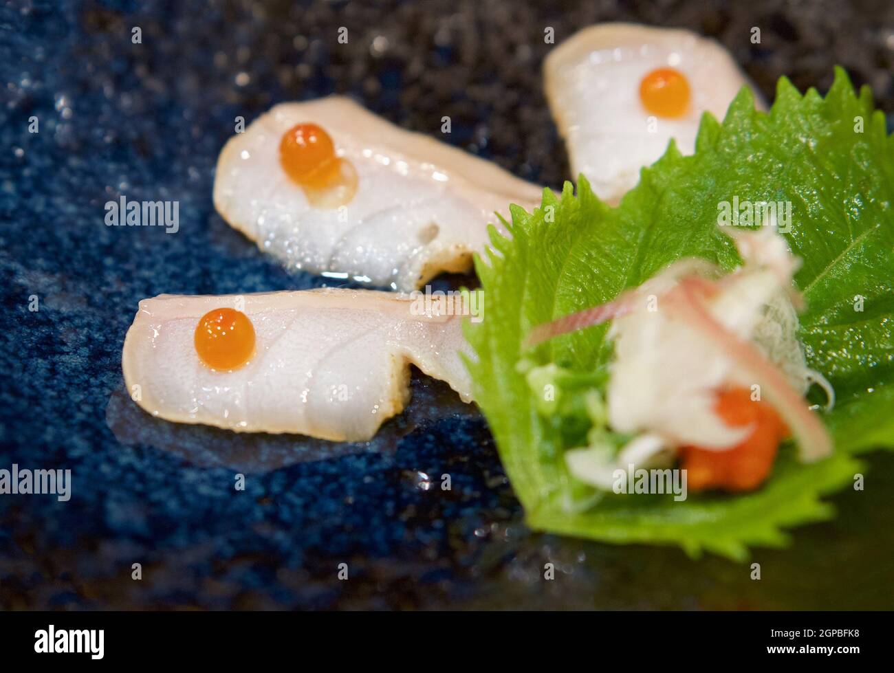 Aburi white fish sliced on top with salmon roe served on dark blue ...