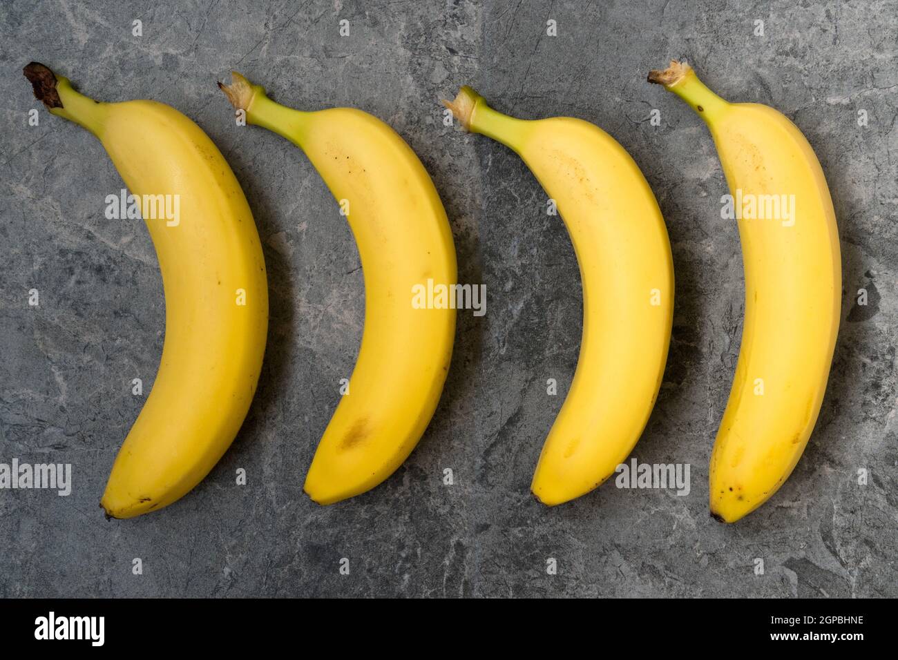 Four bananas placed on the dark stone background Stock Photo - Alamy