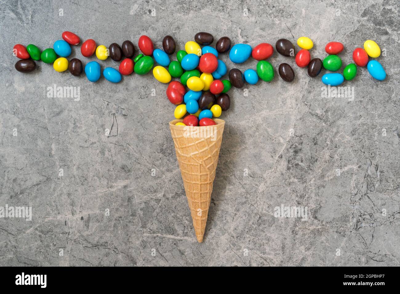 Wafer horn with colored candy on a stone background. Top view, copy ...