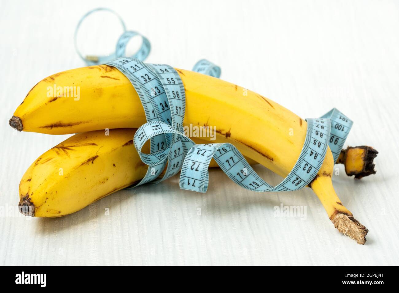 Closeup view of bananas and measuring tape on white wooden background ...