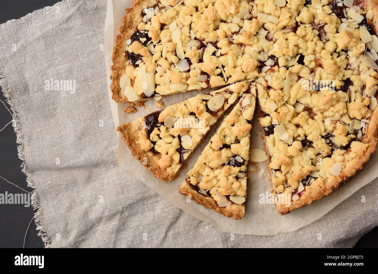 baked round crumble pie with plum cut into pieces on a black background ...
