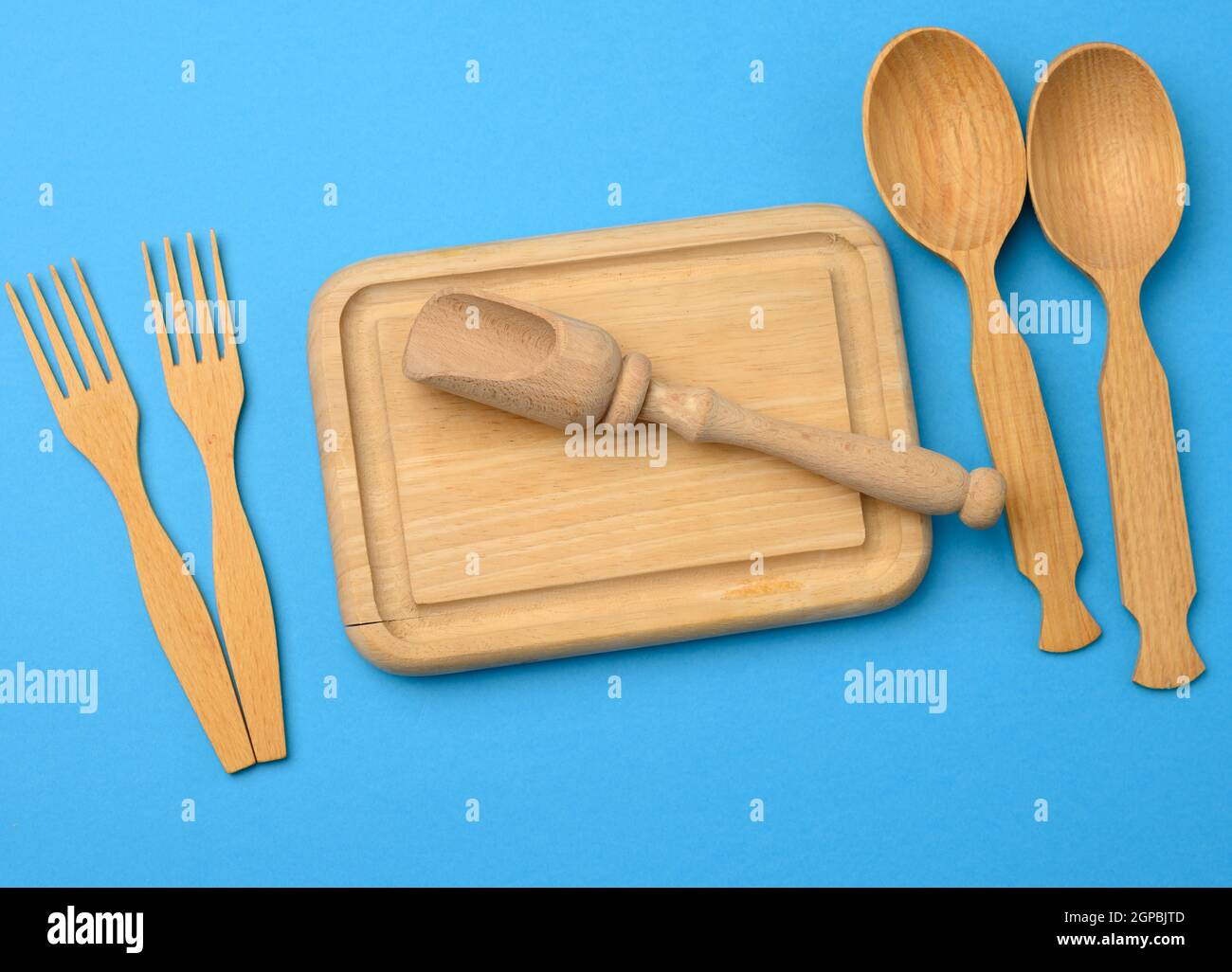 wooden spoons, forks and rectangular cutting board on a blue background ...