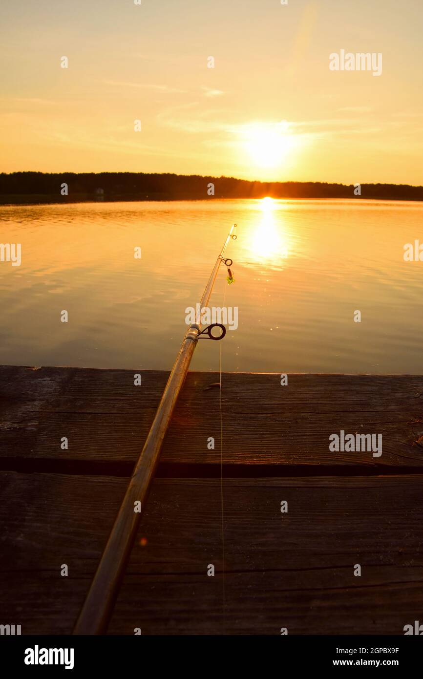 Close up high angle view of fishing rod on wooden pier at sunset hour ...