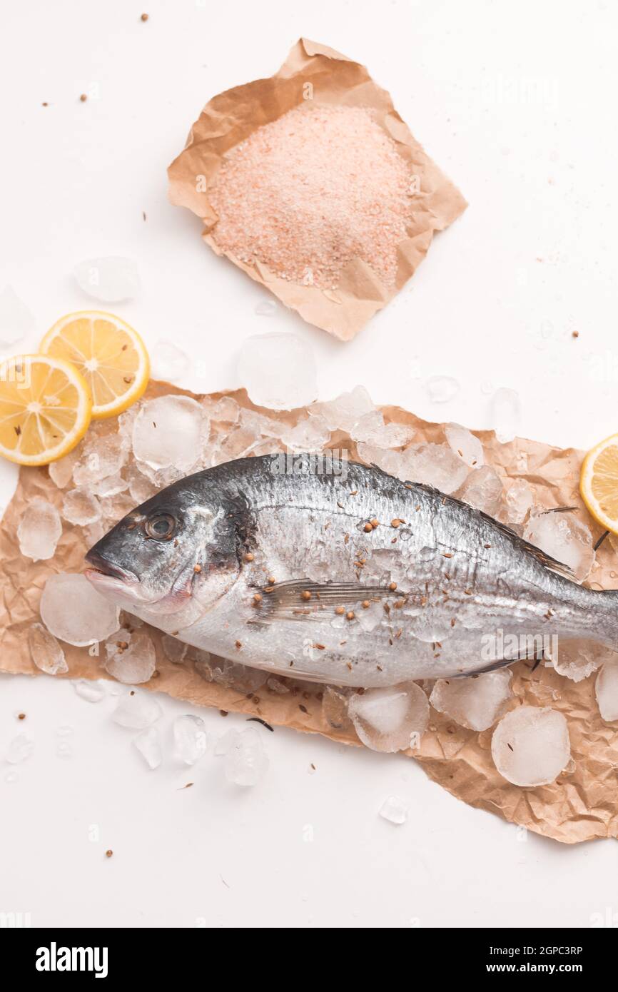 Raw dorada fish or gilt-head bream on ice with lemon and salt over ...