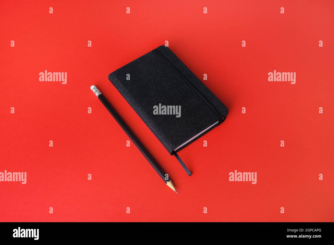 Black notebook and pencil on red paper background. Space for your text ...