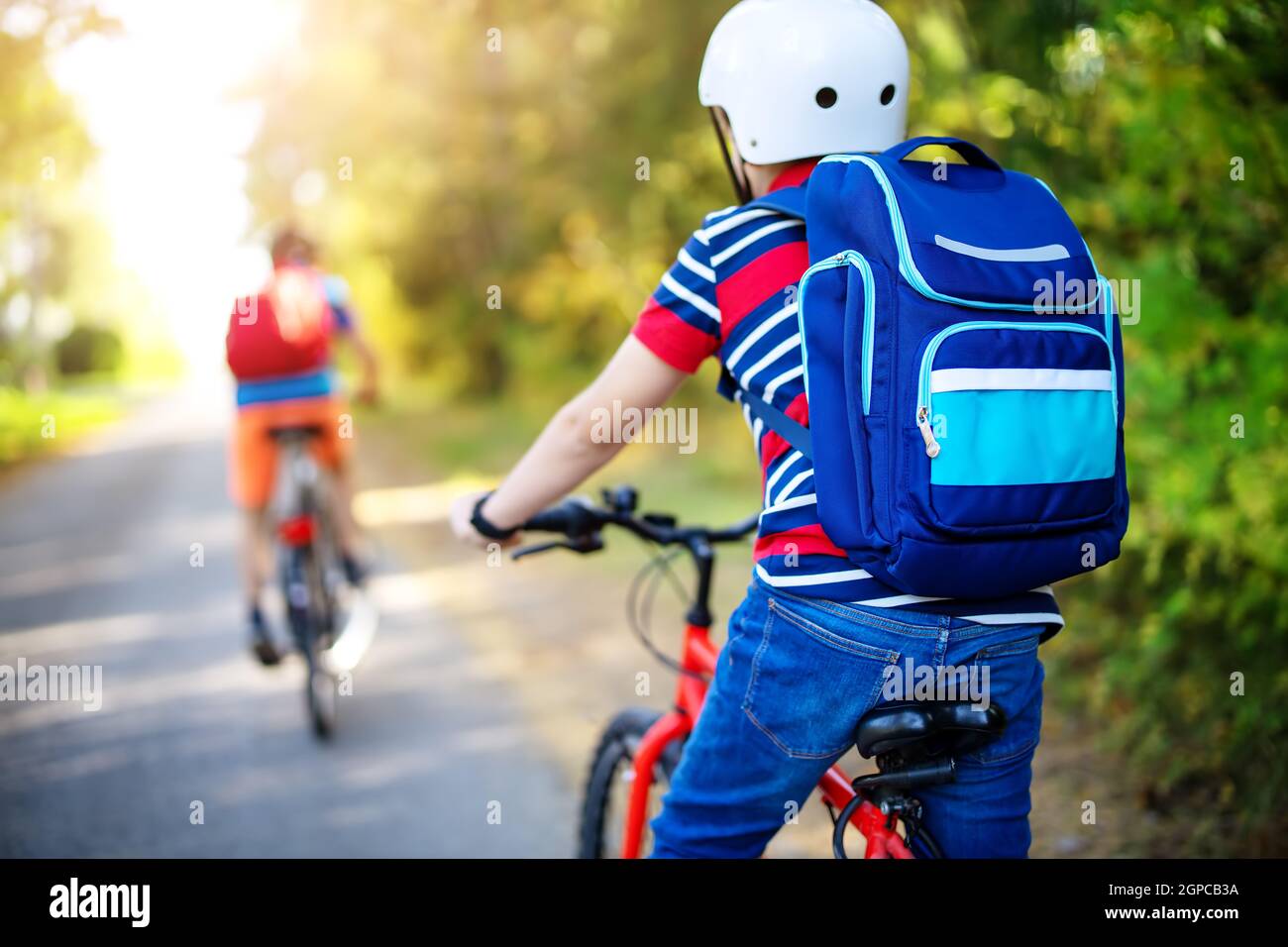 Children with rucksacks riding on bikes in the park near school. Pupils ...
