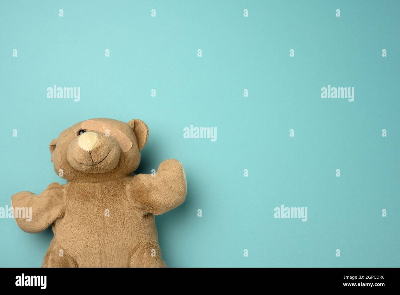 old teddy bear with a band-aid on the eye lies on a blue background ...