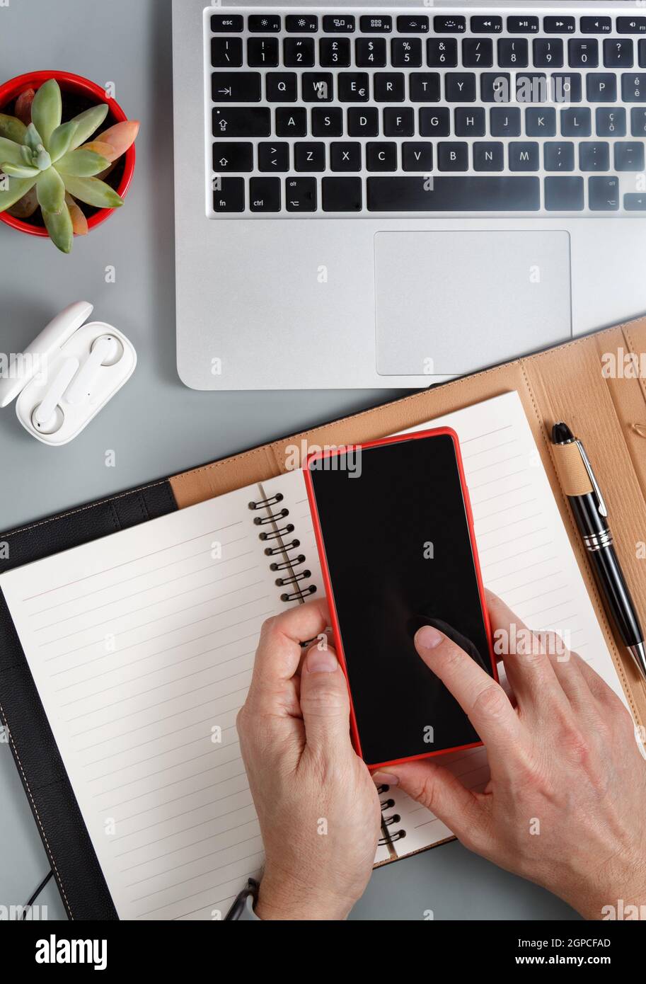 Man writing in agenda and using cell phone on a grey office desk top ...
