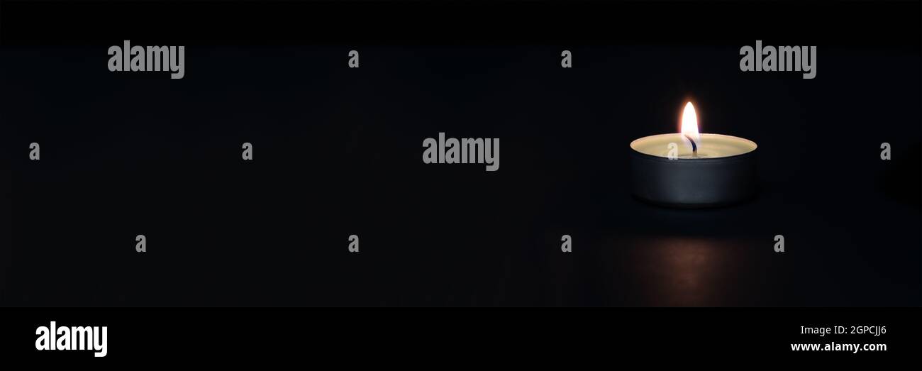 A burning candle on a dark background with a flare in the foreground ...